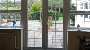 Quarto com uma grande porta de vidro deslizante que dá para um pátio, um radiador, um tapete azul e uma pequena mesa com um relógio.