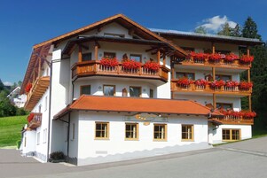 Um edifício de vários andares com varandas decoradas com flores vermelhas, uma placa indicando um restaurante, e um céu claro.