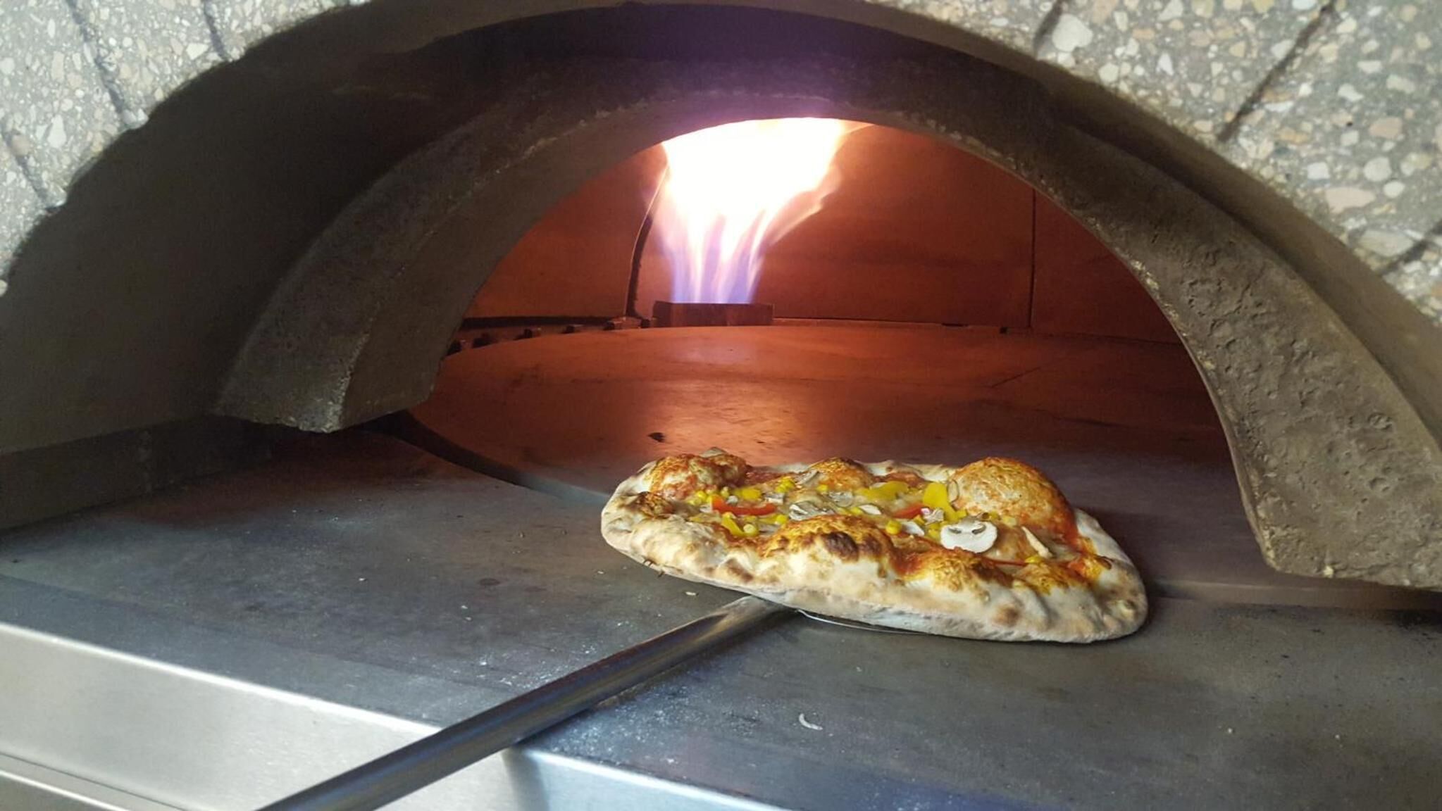 Pizza dentro de um forno de tijolos com chama visível.