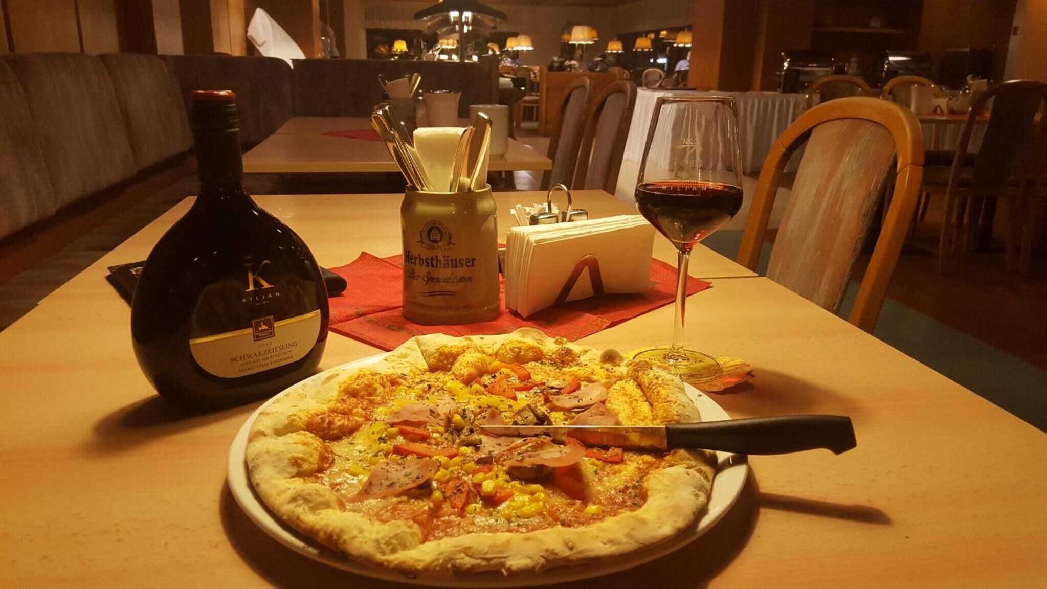 Uma mesa de jantar com pizza, uma garrafa de vinho e uma taça de vinho em um restaurante.