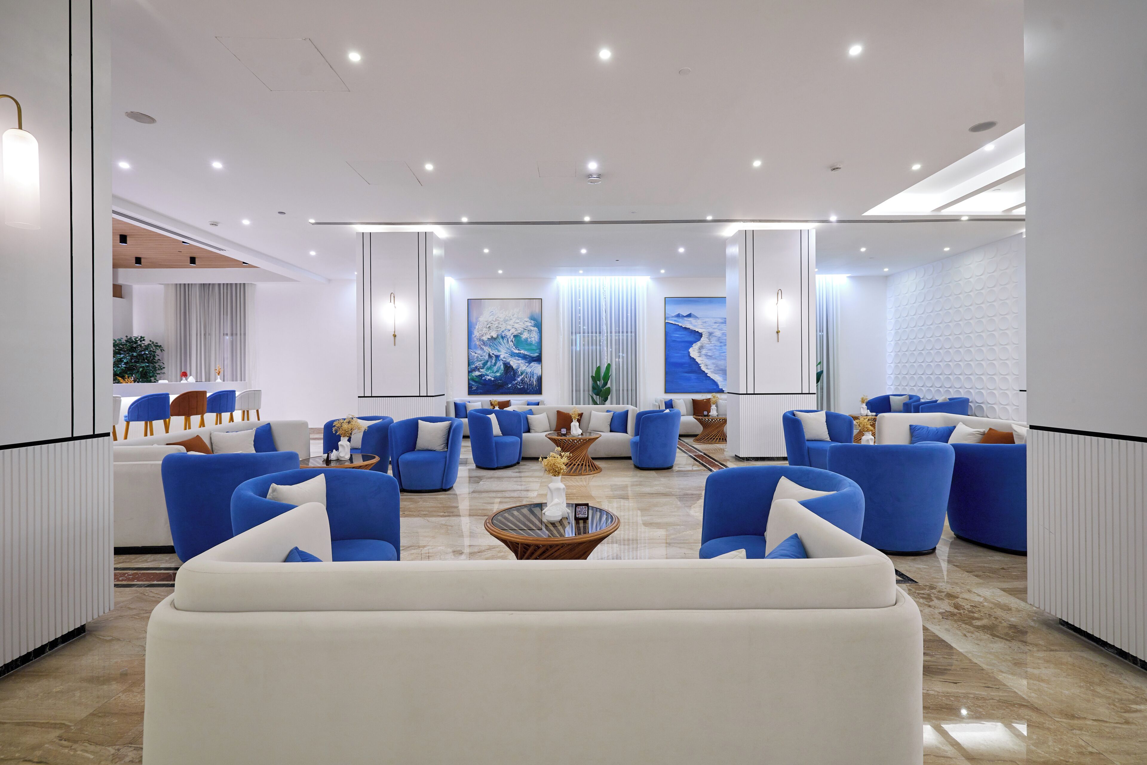 Um hall de hotel moderno com área de estar central, janelas amplas e piso de mármore.