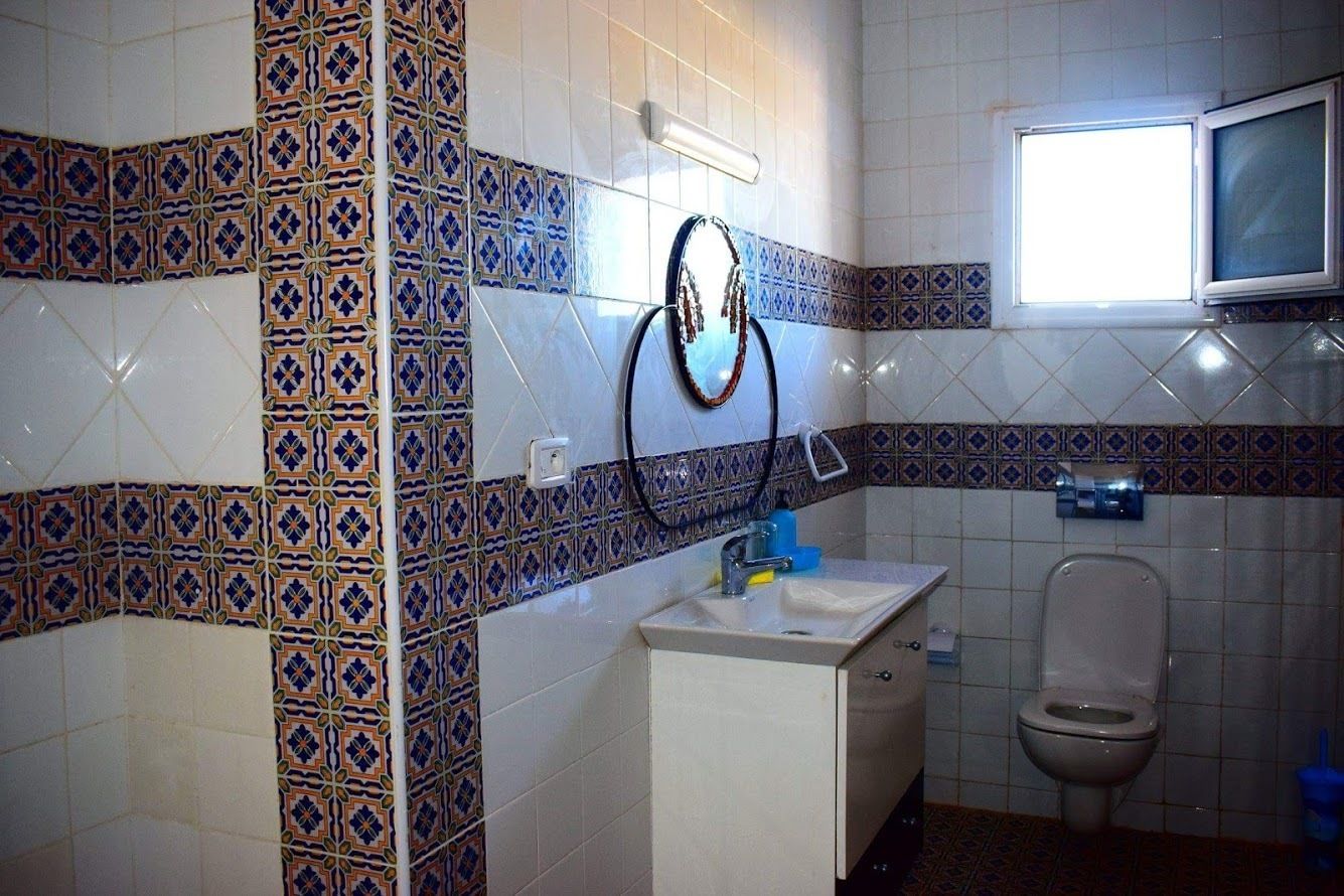Casa de banho com azulejos estampados, lavatório, sanita e janela.