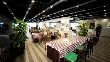 Um restaurante com mesas cobertas por toalhas xadrez, cadeiras e plantas em vasos.