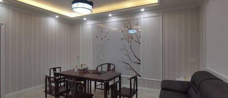 Uma área de refeições com uma mesa e cadeiras de madeira escura, um lustre e uma parede com painéis verticais.