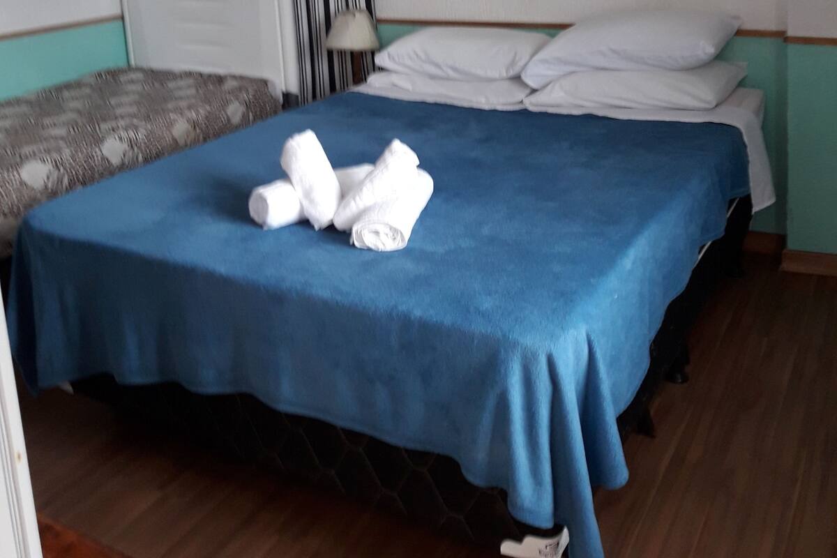 Quarto de hotel com cama, uma cadeira, uma luminária e janela com cortinas.