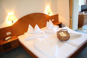 Quarto de hotel com cabeceira de madeira, duas luminárias de cabeceira, televisão de tela plana, mesa de cabeceira com telefone e cesto de vime na cama.