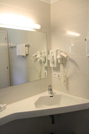 Casa de banho com uma pia branca, um espelho e dois secadores de cabelo fixados na parede.