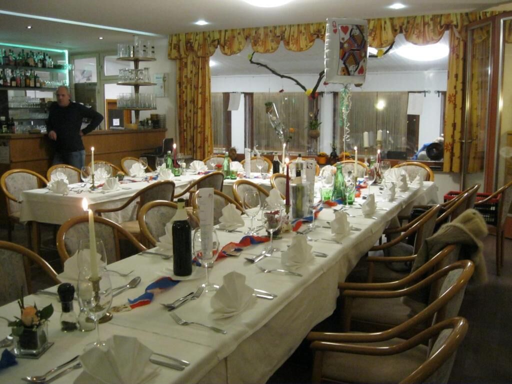 Uma longa mesa de jantar posta com cadeiras, velas e copos, com um bar ao fundo.
