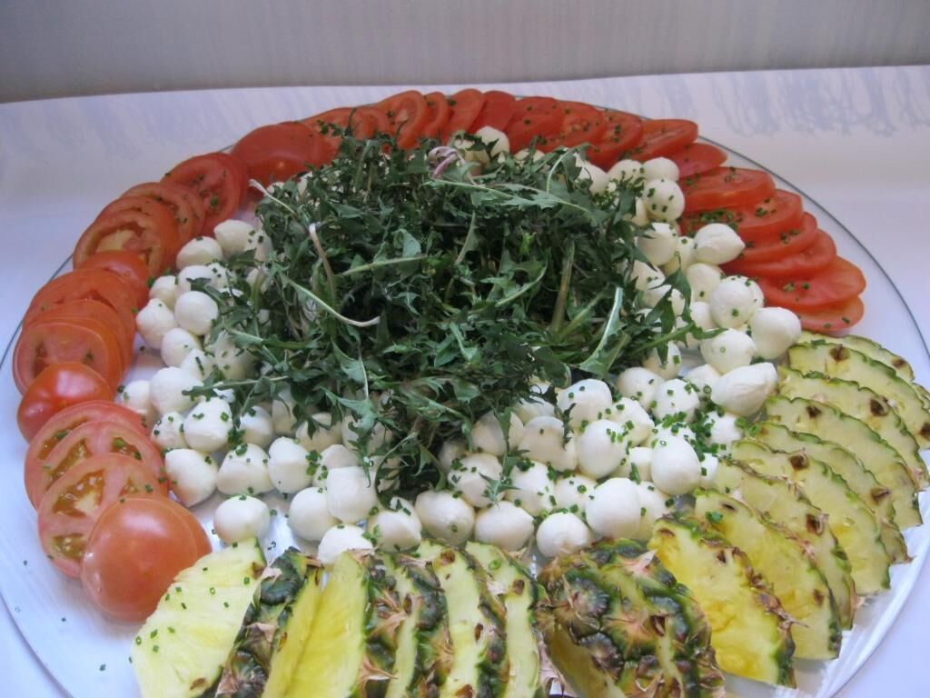 Um prato com fatias de tomate, bolinhas de mussarela, rúcula e abobrinha grelhada.