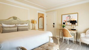Quarto de hotel com uma cama grande, uma escrivaninha, uma cadeira, um banco e um quadro pendurado na parede.