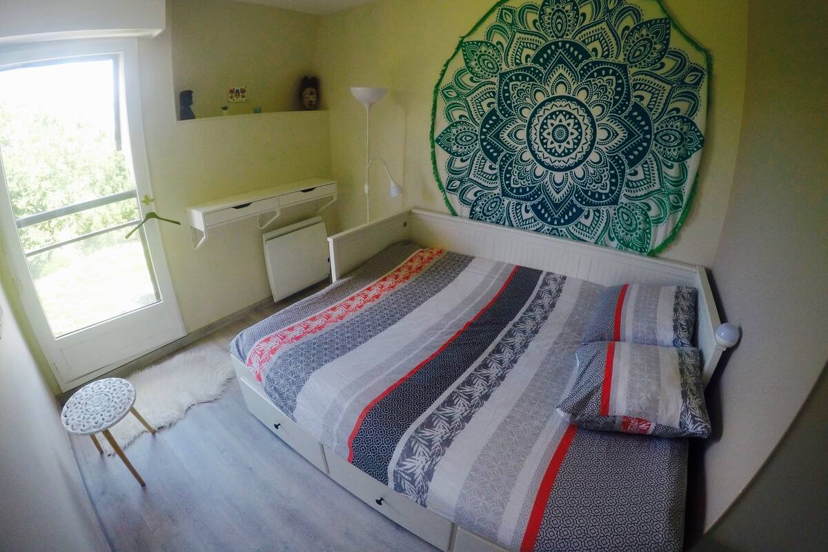 Quarto com cama, janela, mesa de cabeceira, abajur e tapeçaria na parede.