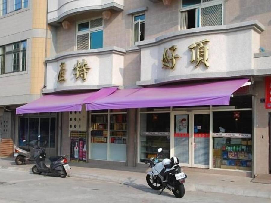 Edifício com fachada e toldo roxo. Scooters e uma motocicleta estacionados em frente.