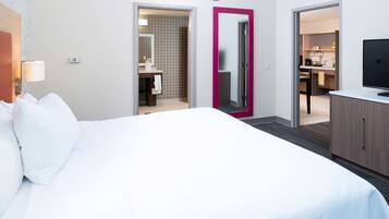 Quarto de hotel com uma cama grande, banheiro com espelho e cozinha compacta.