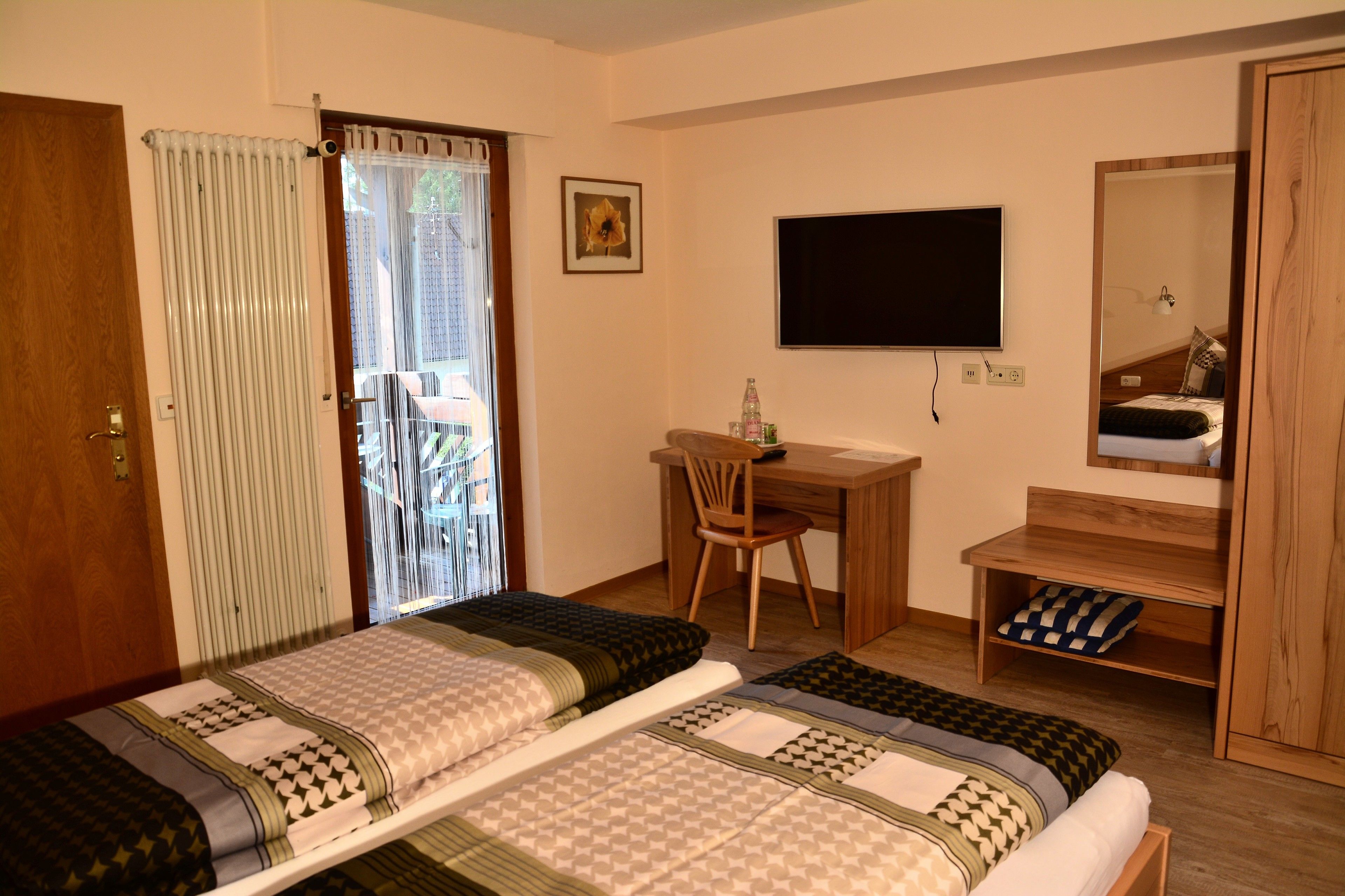 Quarto com duas camas, uma escrivaninha, uma cadeira, uma televisão e um guarda-roupa.