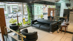 Um lobby moderno com um sofá de couro, uma cadeira preta e uma pequena mesa com uma planta.