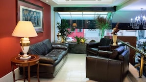 Um lobby de hotel moderno com sofás de couro, uma luminária de mesa e uma janela grande com vista para o exterior.