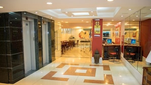 Um lobby de hotel com design moderno, apresentando um elevador de vidro, uma área de refeições e postos de computadores.