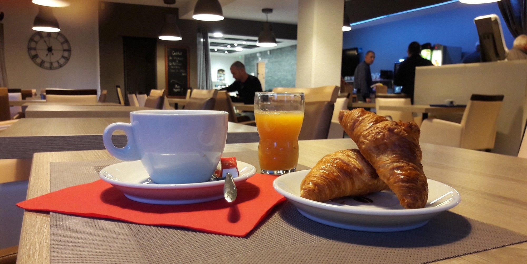 Mesa com xícara, copo de suco de laranja e croissants para o café da manhã.