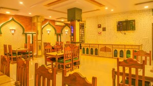 Um restaurante com mesas e cadeiras de madeira, uma parede de tijolos e iluminação decorativa.