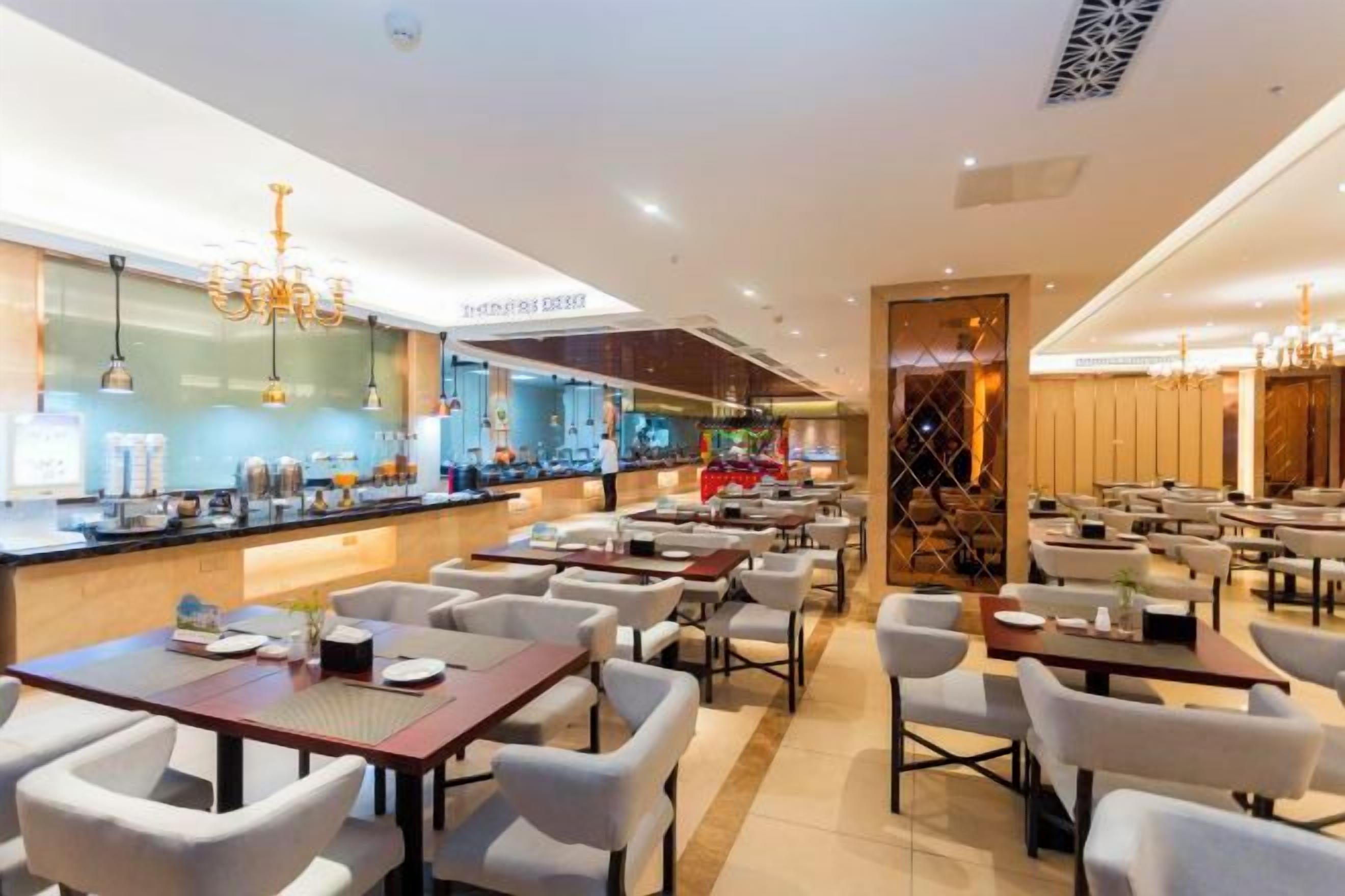 Restaurante moderno de hotel, com várias mesas e cadeiras, área de bar e vista para a paisagem urbana.