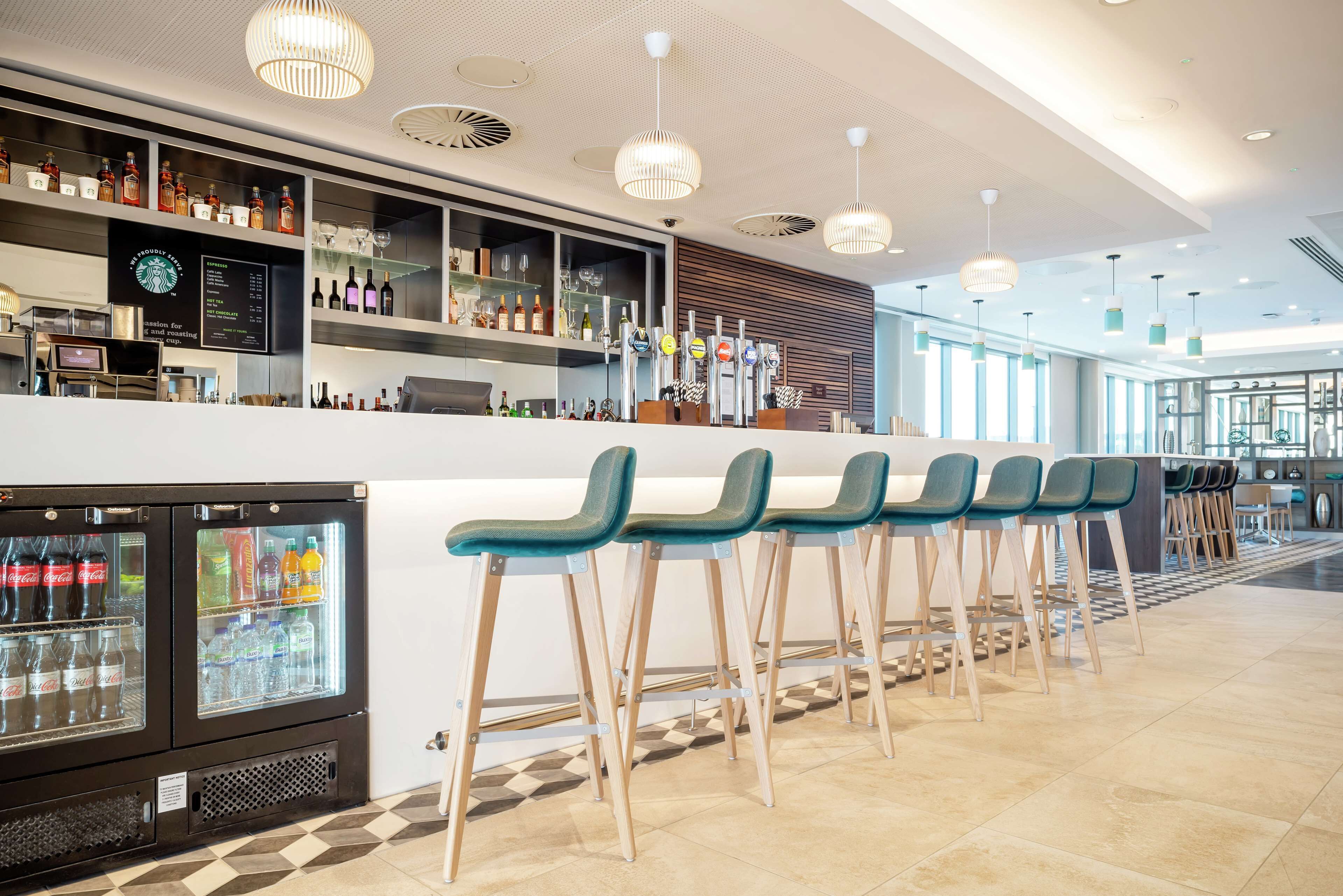 Uma área de bar moderna com balcão, estantes de bebidas e banquetas.