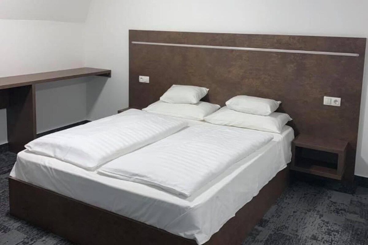 Quarto individual com uma cama de solteiro, cabeceira de madeira, mesa de cabeceira e piso coberto por carpete.