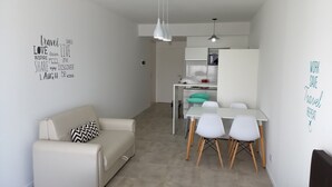 Um espaço de estar moderno e funcional, com sofá, mesa de jantar e cadeiras. As paredes decoradas exibem frases motivacionais.