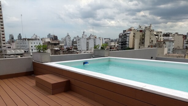 Piscina no terraço com deck de madeira e vista para a cidade.