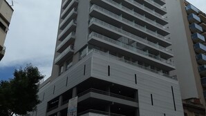 Edifício de vários andares com design arquitetônico moderno, destacando uma entrada imponente com fachada de vidro e uma placa.