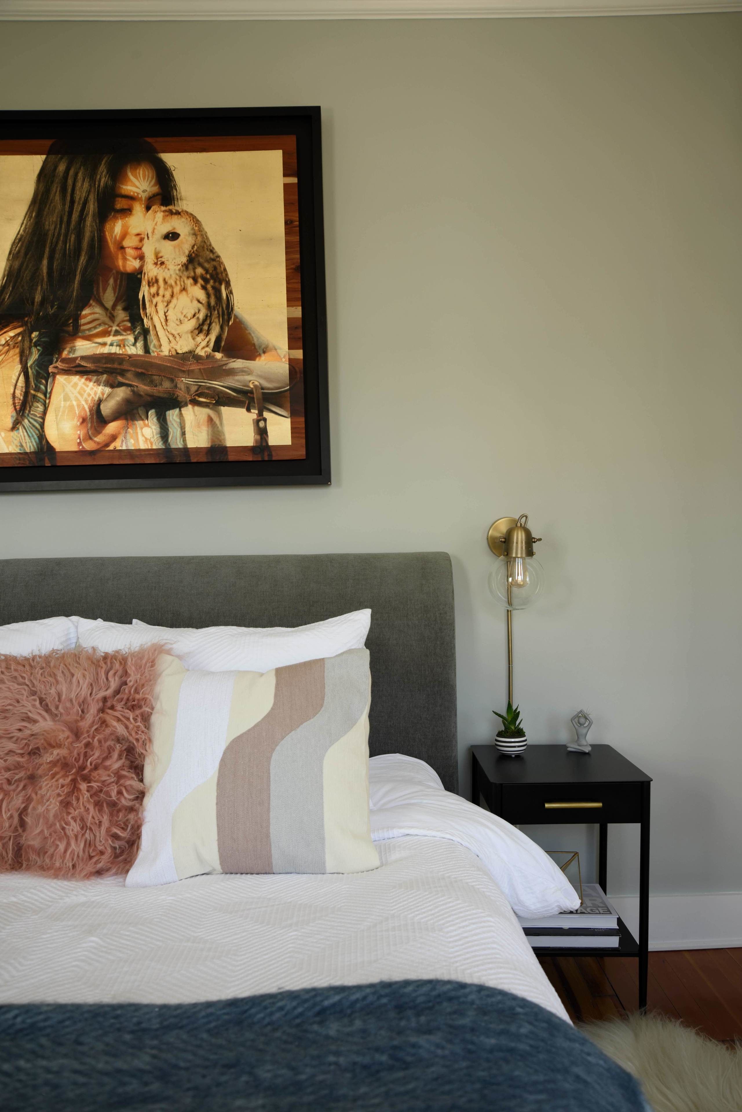 Quarto com cama, almofadas, um quadro emoldurado, mesa de cabeceira e abajur.