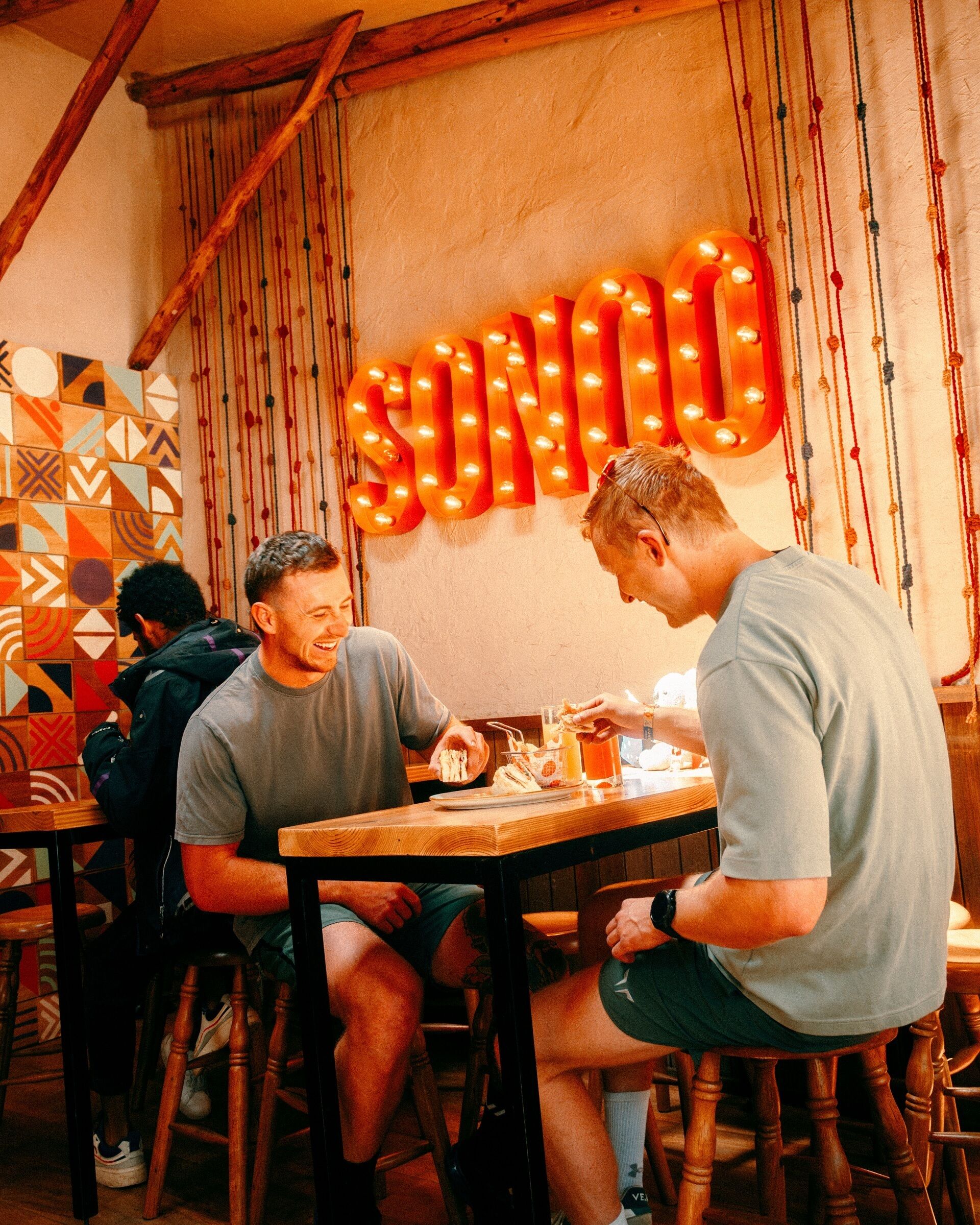 Interior de restaurante com mesa de madeira, cadeiras e um letreiro de neon.