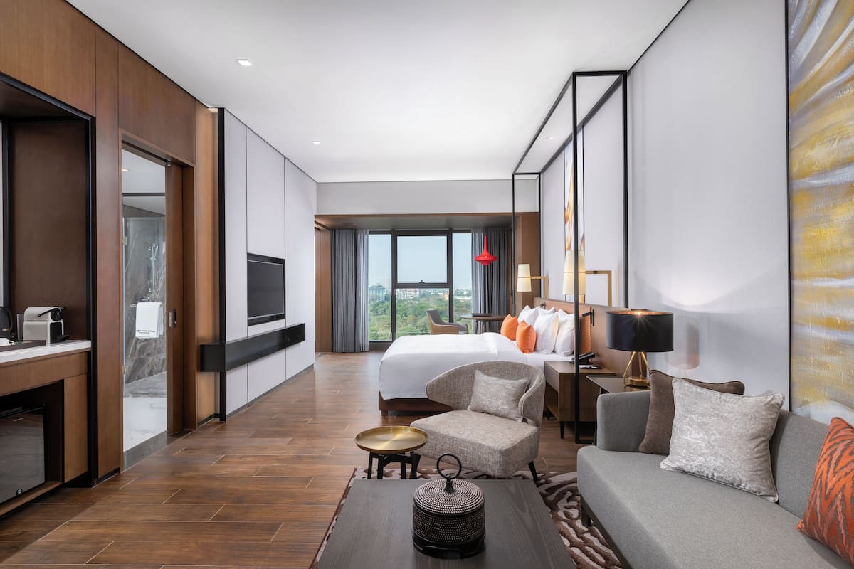 Quarto de hotel moderno com uma cama grande, um sofá, uma mesa de centro e uma escrivaninha com computador.