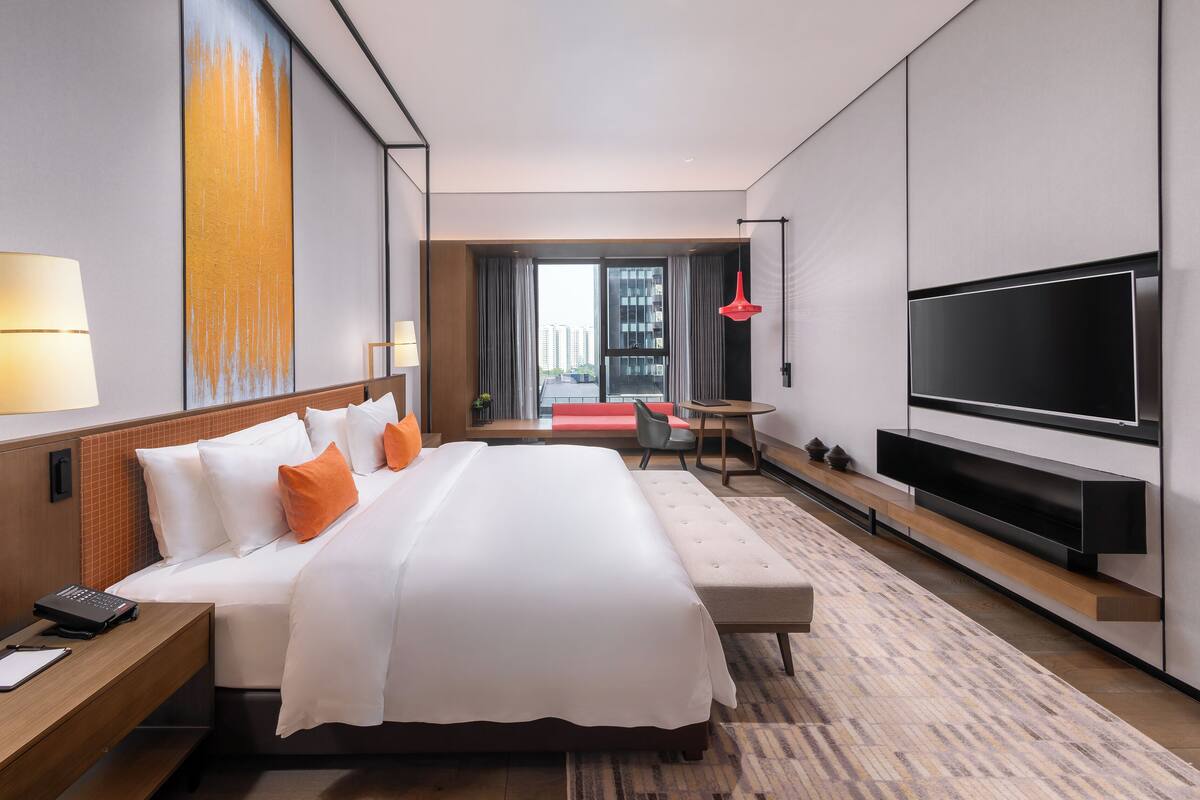 Quarto de hotel com uma cama grande, uma escrivaninha com computador, televisão e vista da cidade pela janela.