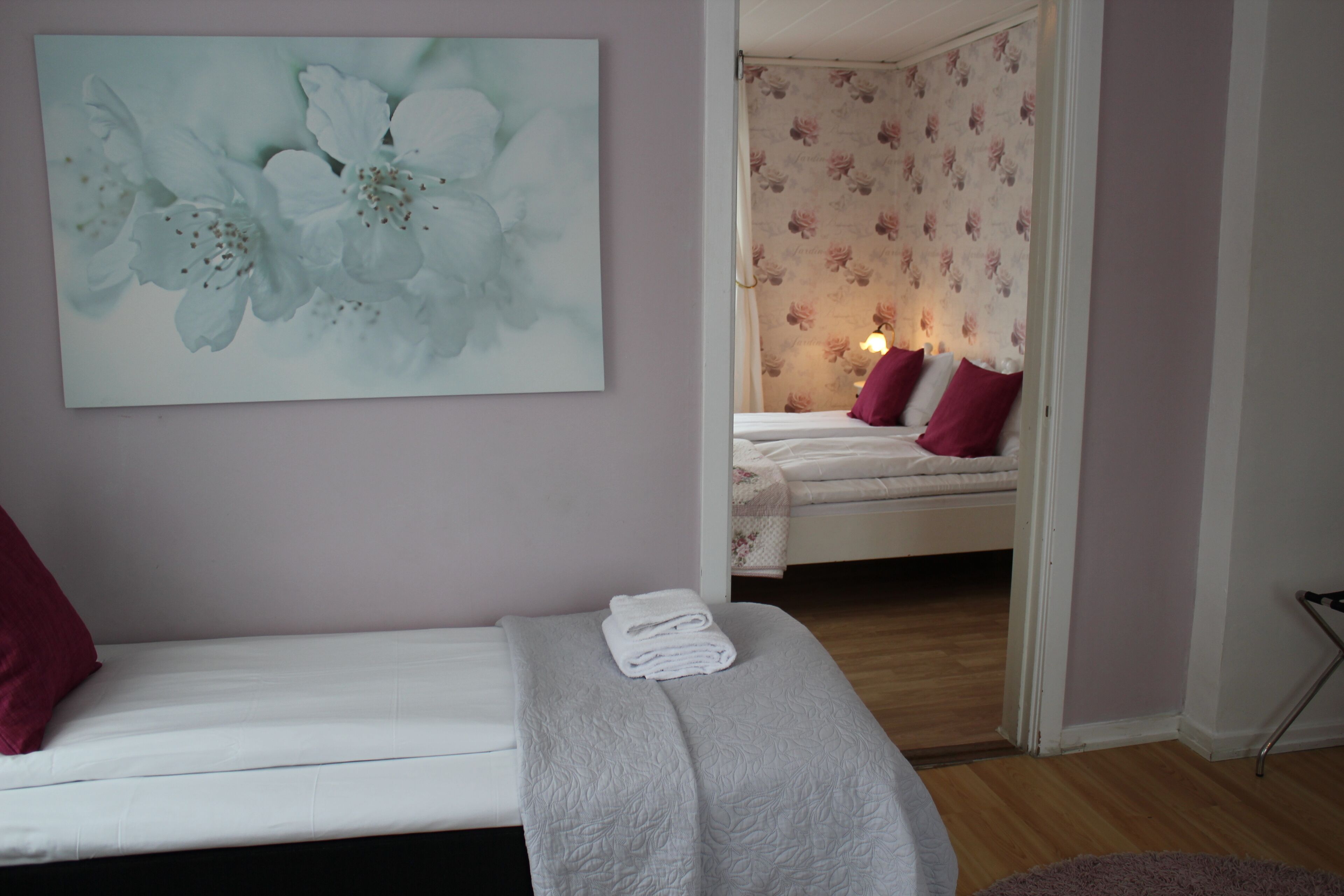 Quarto com cama, um quadro pendurado na parede e porta que dá para outro espaço.