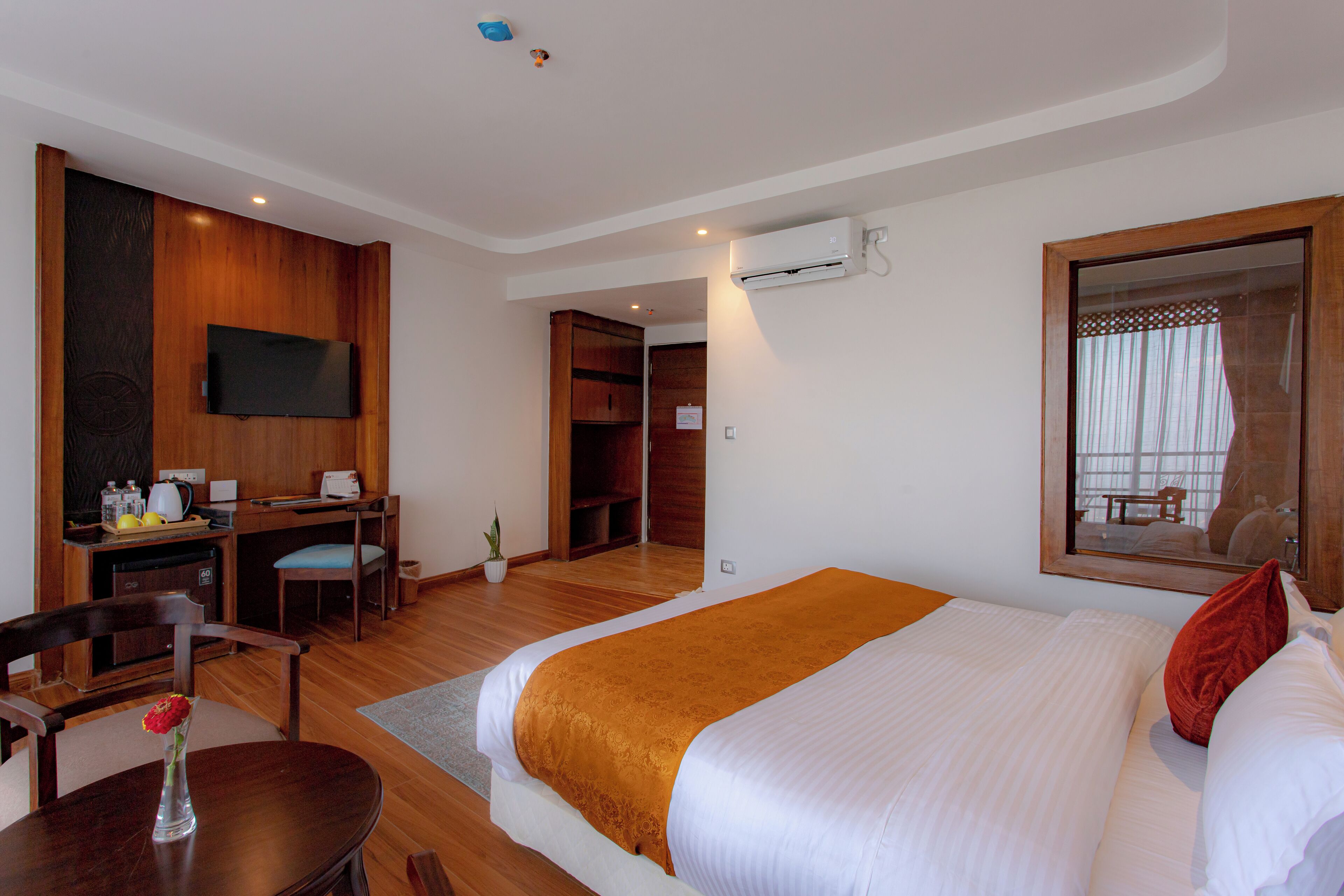 Quarto de hotel com uma cama, uma escrivaninha com cadeira, televisão e ar condicionado.