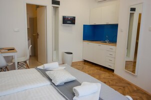 Quarto de hotel com cama, escrivaninha, pequeno espaço de cozinha e banheiro.