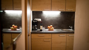 Uma cozinha compacta com armários de madeira, cafeteira, uma garrafa de vinho e uma fruteira.