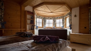 Quarto de cabana de madeira com duas camas, teto de madeira e janela com cortinas.