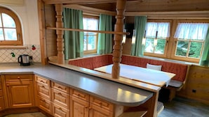 Cozinha com armários de madeira, bancada de granito, um banco embutido e grandes janelas com cortinas.