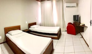 Quarto com duas camas de solteiro, uma escrivaninha com cadeira, televisão e ar condicionado.