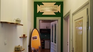 Um corredor com parede verde decorativa, prateleiras de madeira, um espelho e uma porta que dá para uma cozinha.