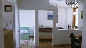 Quarto com piso de madeira, cama com roupa de cama listrada, um banco e uma pequena mesa com garrafa e copos.