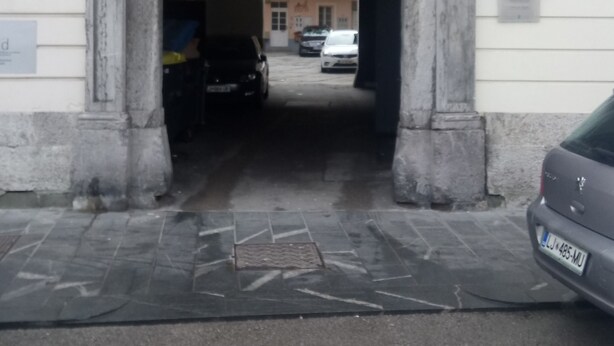 Uma entrada com arco de pedra, chão pavimentado e um edifício ao fundo.