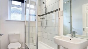 Casa de banho moderna com cabine de duche em vidro, sanita branca e lavatório com espelho.