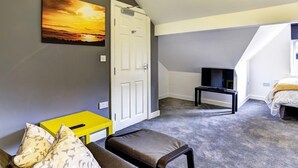 Um quarto aconchegante com parede cinza, mesa amarela, sofá marrom, uma televisão e uma porta.