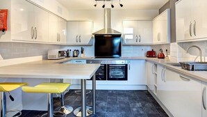 Uma cozinha moderna com armários brancos, eletrodomésticos de aço inoxidável, uma ilha central e um banquinho amarelo.