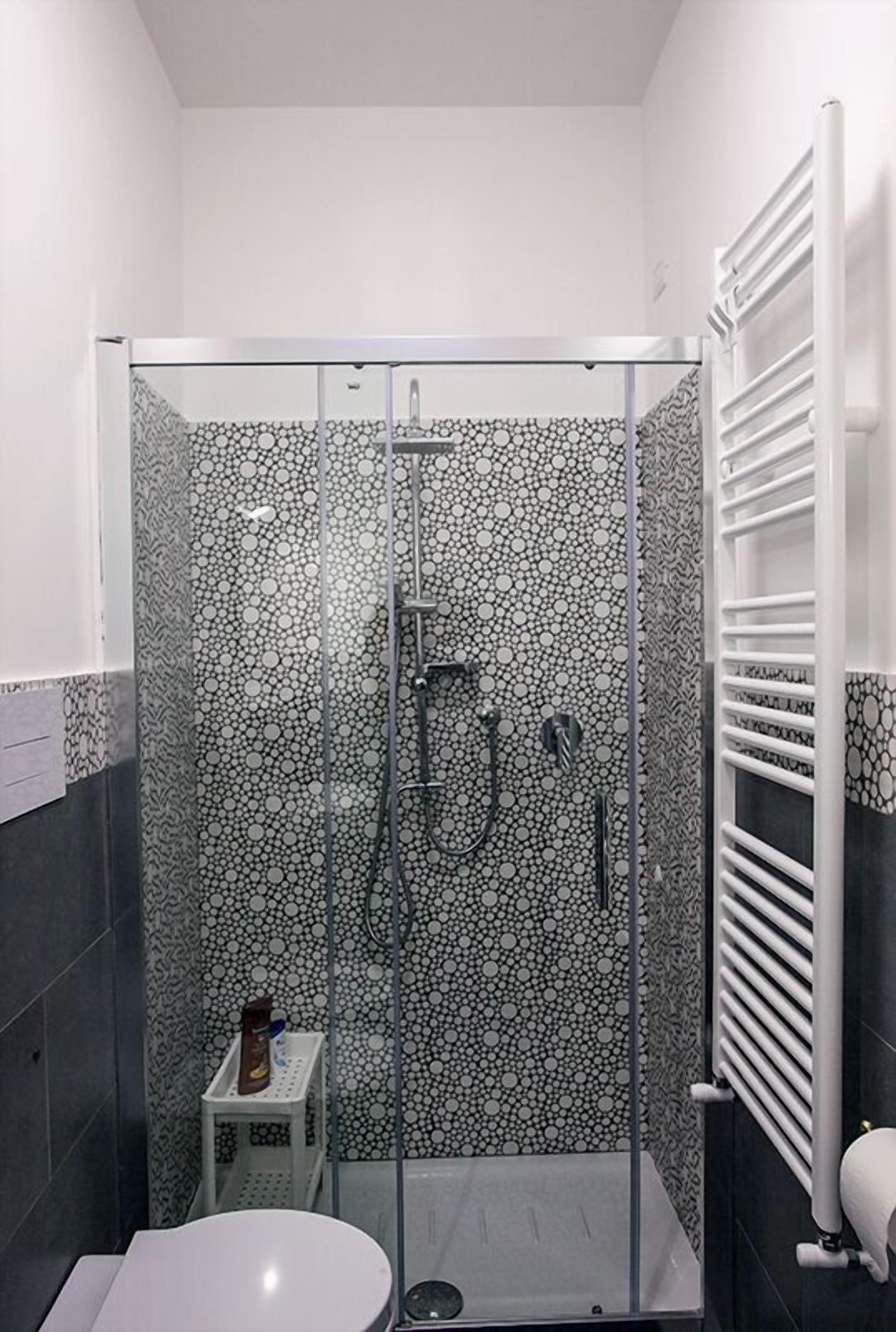 Uma casa de banho moderna com cabine de duche em vidro, sanita branca e porta-toalhas.