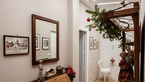 Um corredor com obras de arte emolduradas nas paredes, um aparador de madeira com figuras e um pinheiro de Natal decorado.