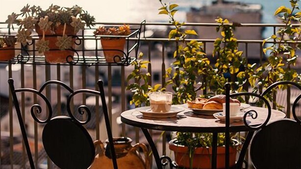 Um terraço com mesa e cadeiras, plantas em vasos e vista para o mar.