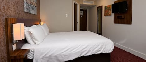 Quarto de hotel com uma cama grande, uma luminária de cabeceira, uma TV de tela plana e um quadro na parede.